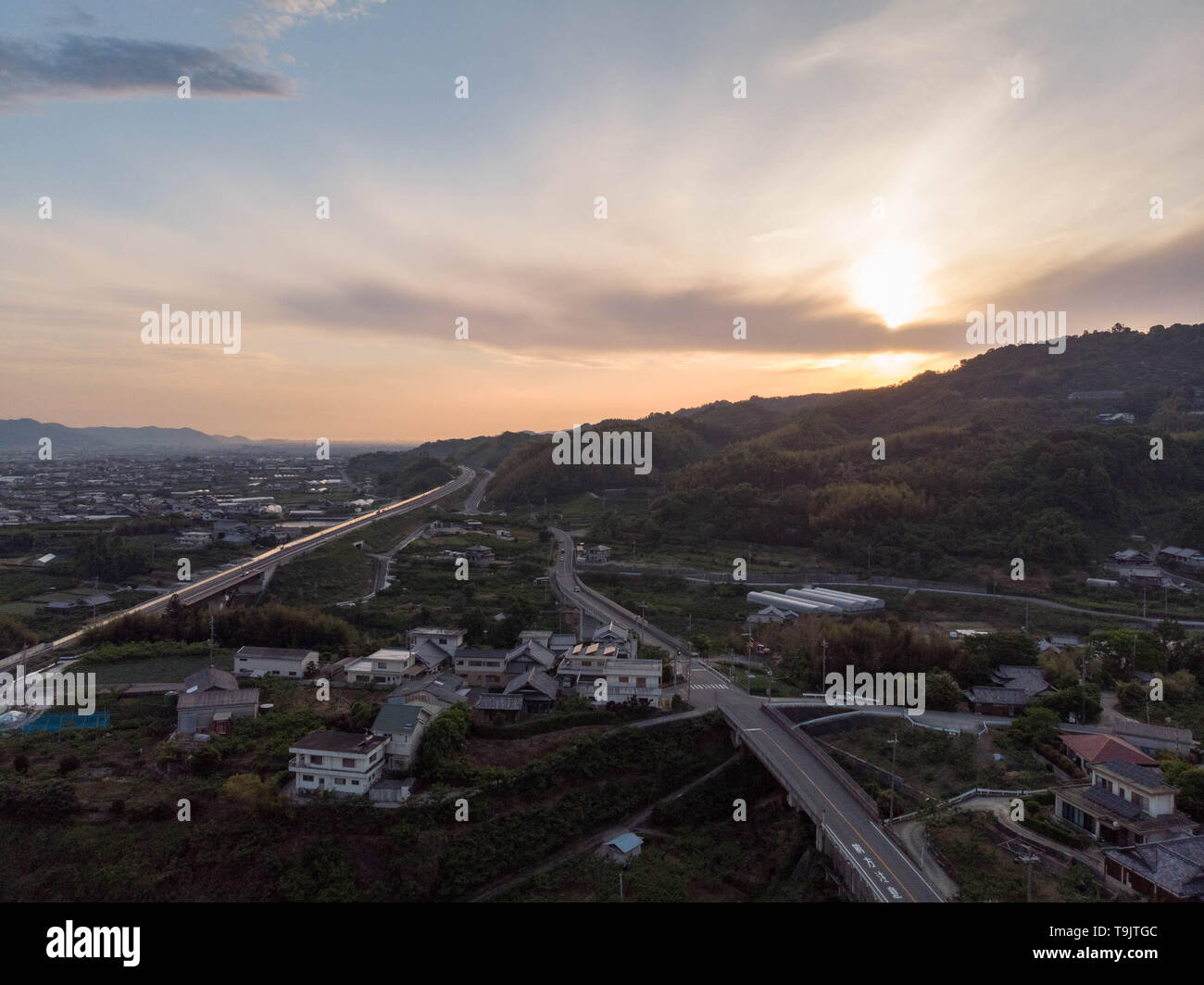 Aerial view of beautiful sunset over empty roadway through small rural ...