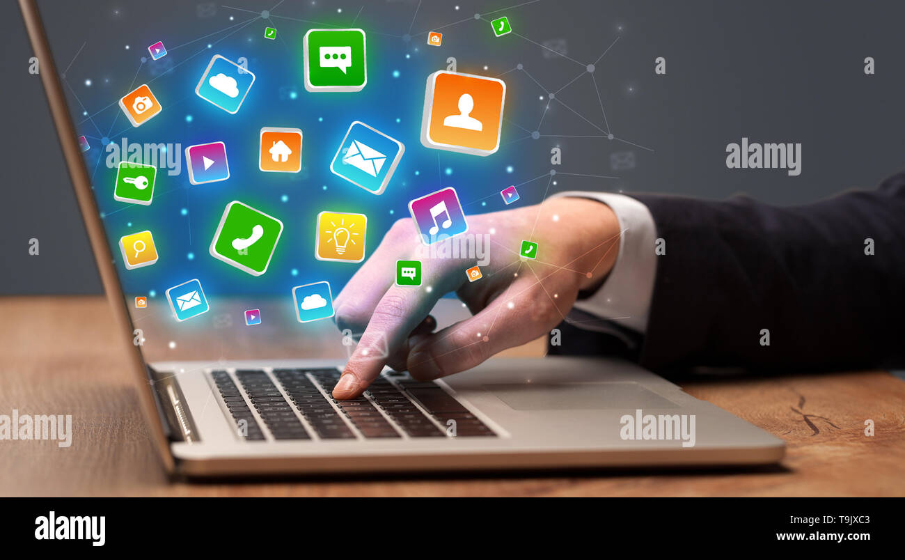 Businessman hand typing on laptop with flying application icons around ...