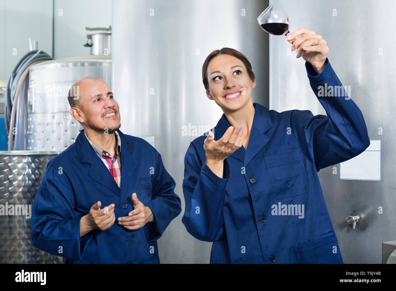 Two cheerful winery workers holding glass of wine in a fermenting ...