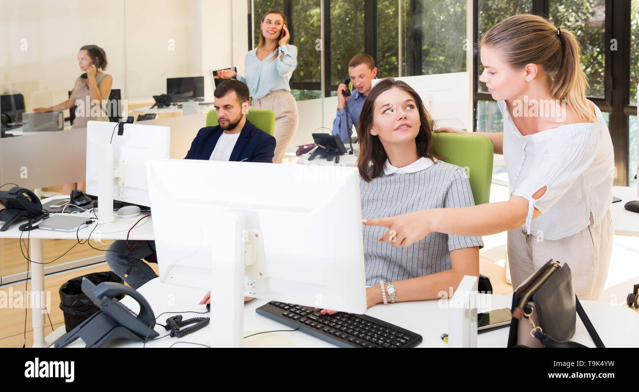 Positive girl helping happy female colleague in work with computer in ...