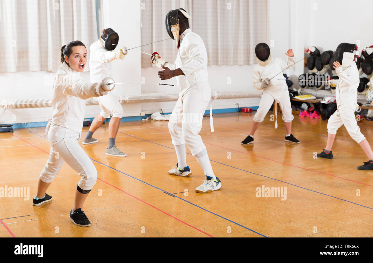 Portrait of emotional young woman wearing fencing uniform practicing with foil in gym Stock ...