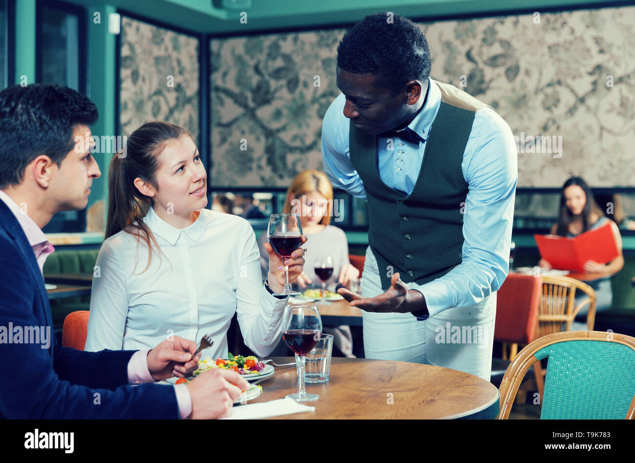 Positive elegant couple talking with polite African American waiter ...