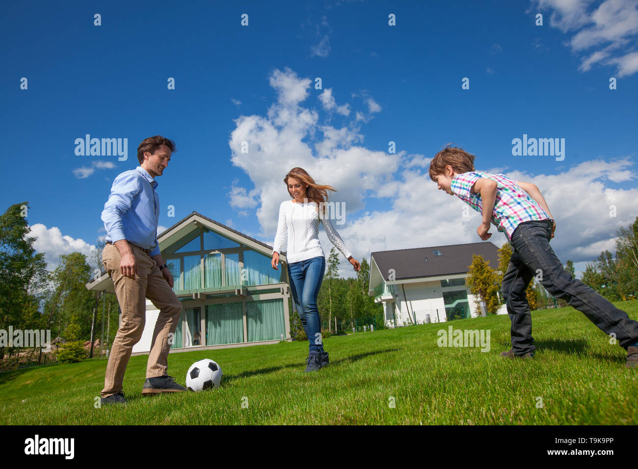 Family with of parents and son playing football on the backyard lawn ...