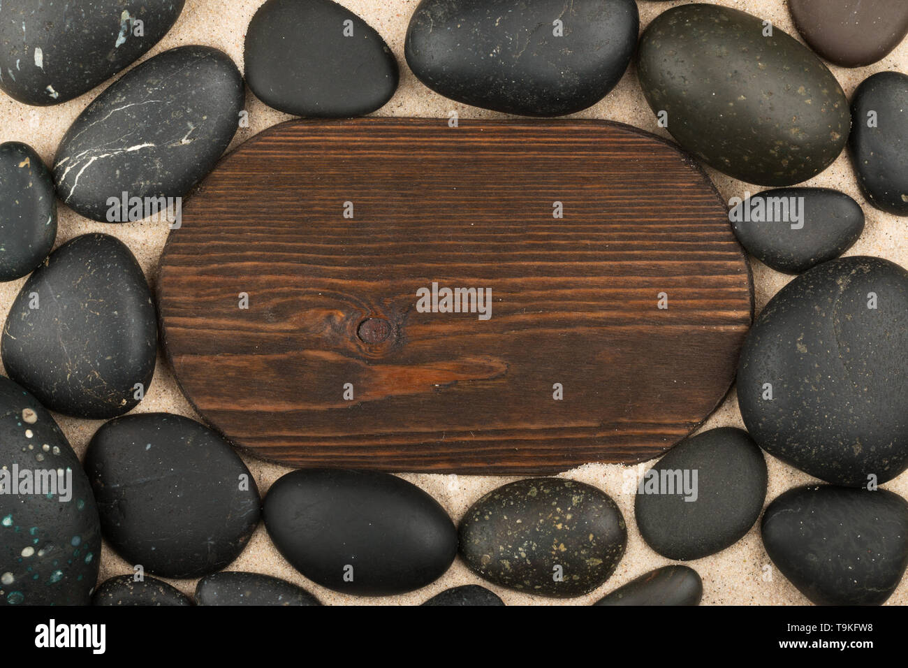 Oval classic frame of dark wood and black stones in the sand. Copy ...