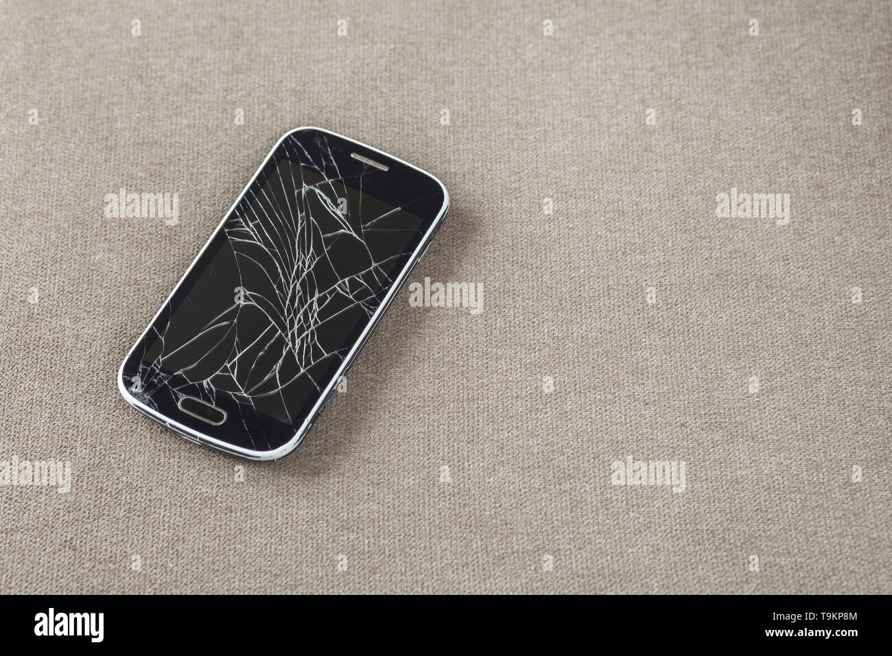 Black old cellphone with cracked screen on light cloth copy space ...