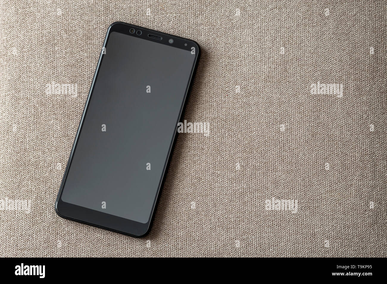 New black modern cellphone isolated on light cloth copy space ...