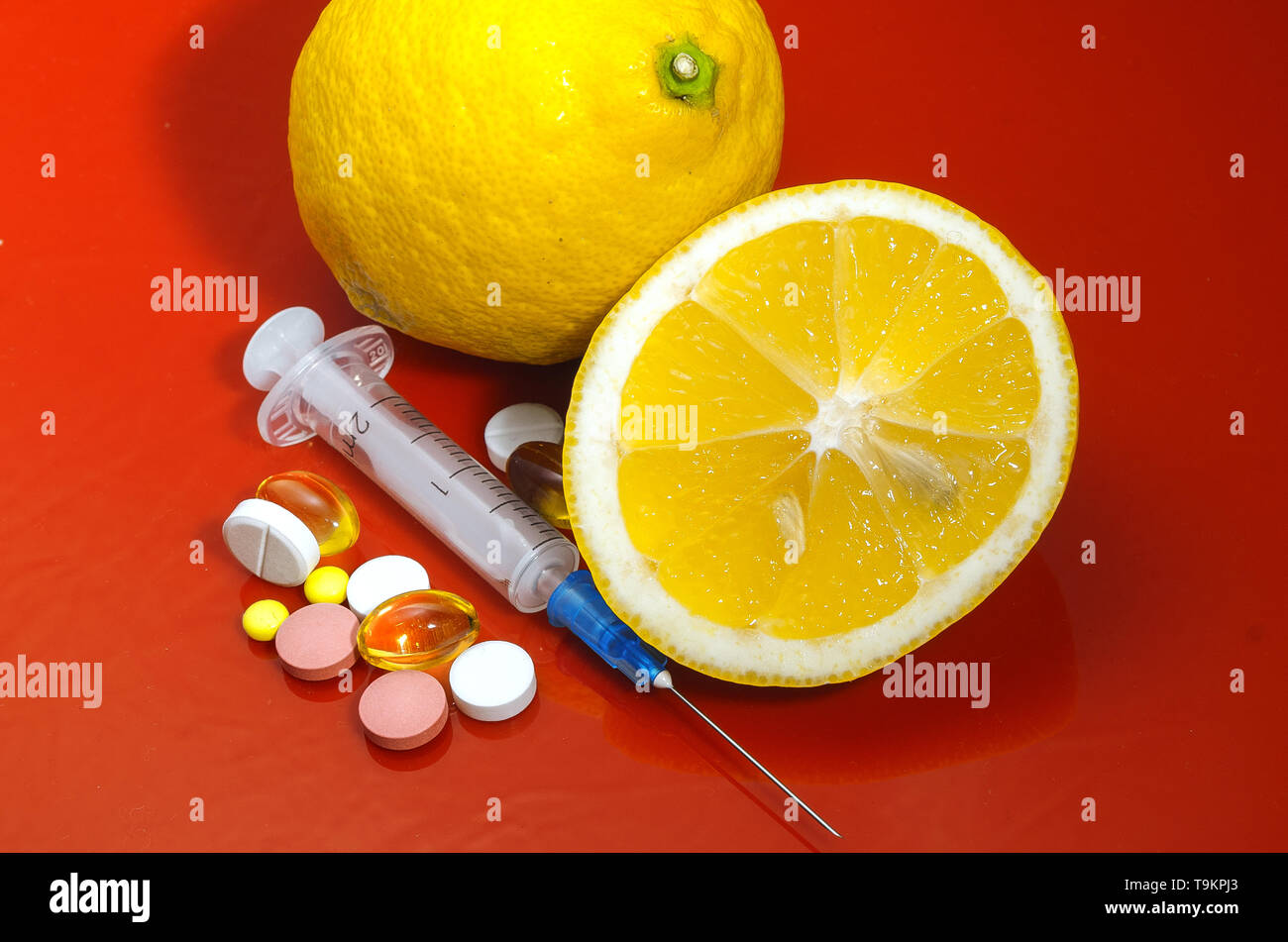 Lemons on a red background with syringes and pills. Medical ...