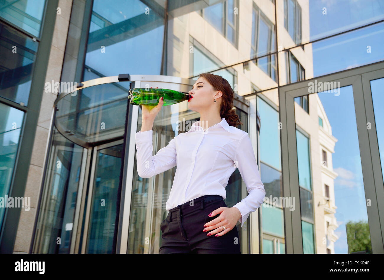 Business lady drinks water from a plastic bottle on the background of ...