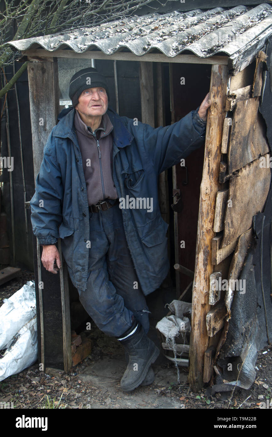 An old man in sloppy clothes stands on the threshold of his own ruined ...