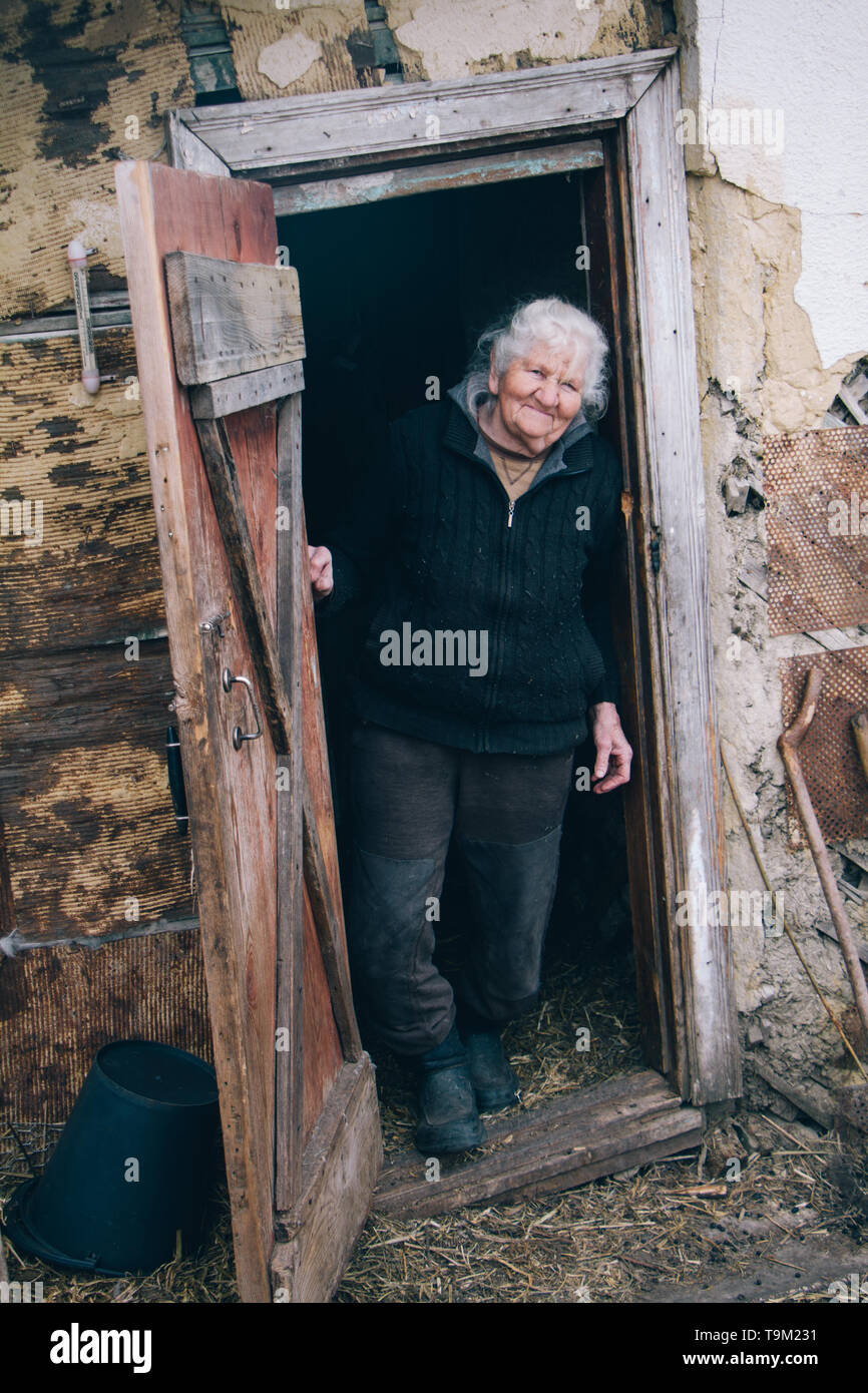 A very old woman with gray hair in old clothes stands on the threshold ...