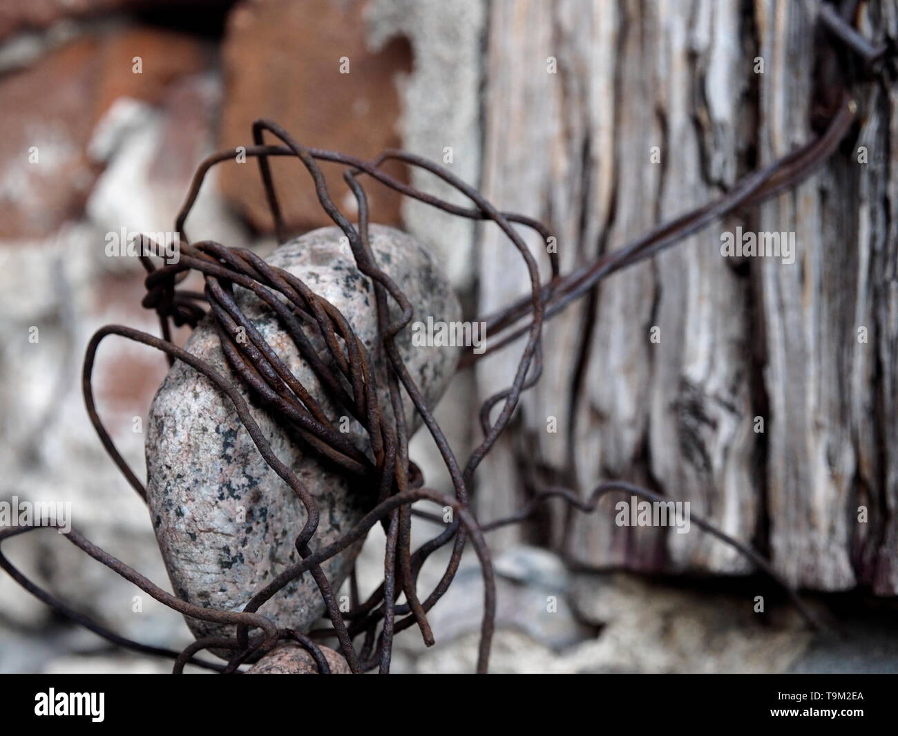 An old rusty wire sticking out from a stone and wood wall is wrapped ...