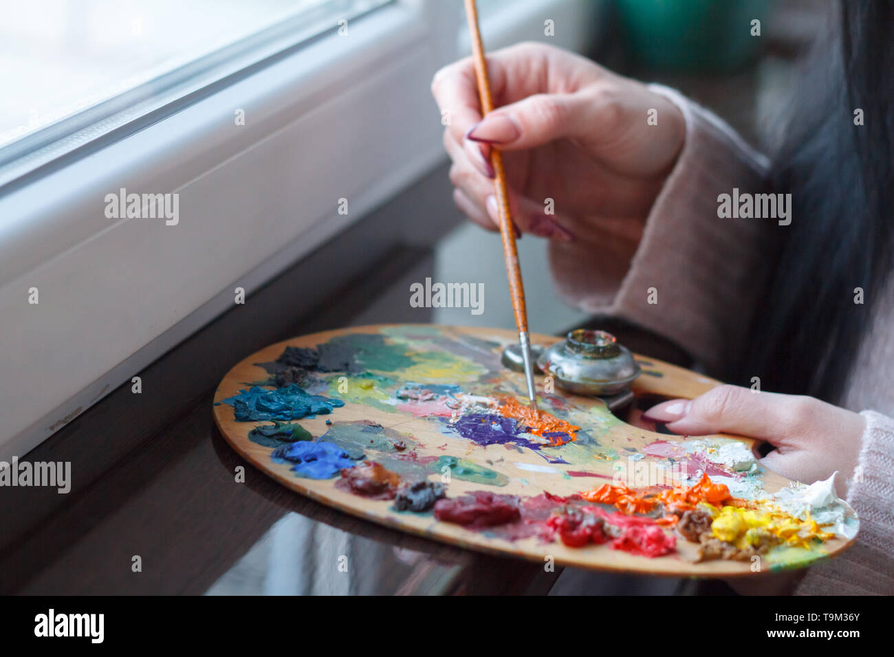 Close-up of female hands mixing paints on a palette with a spatula ...