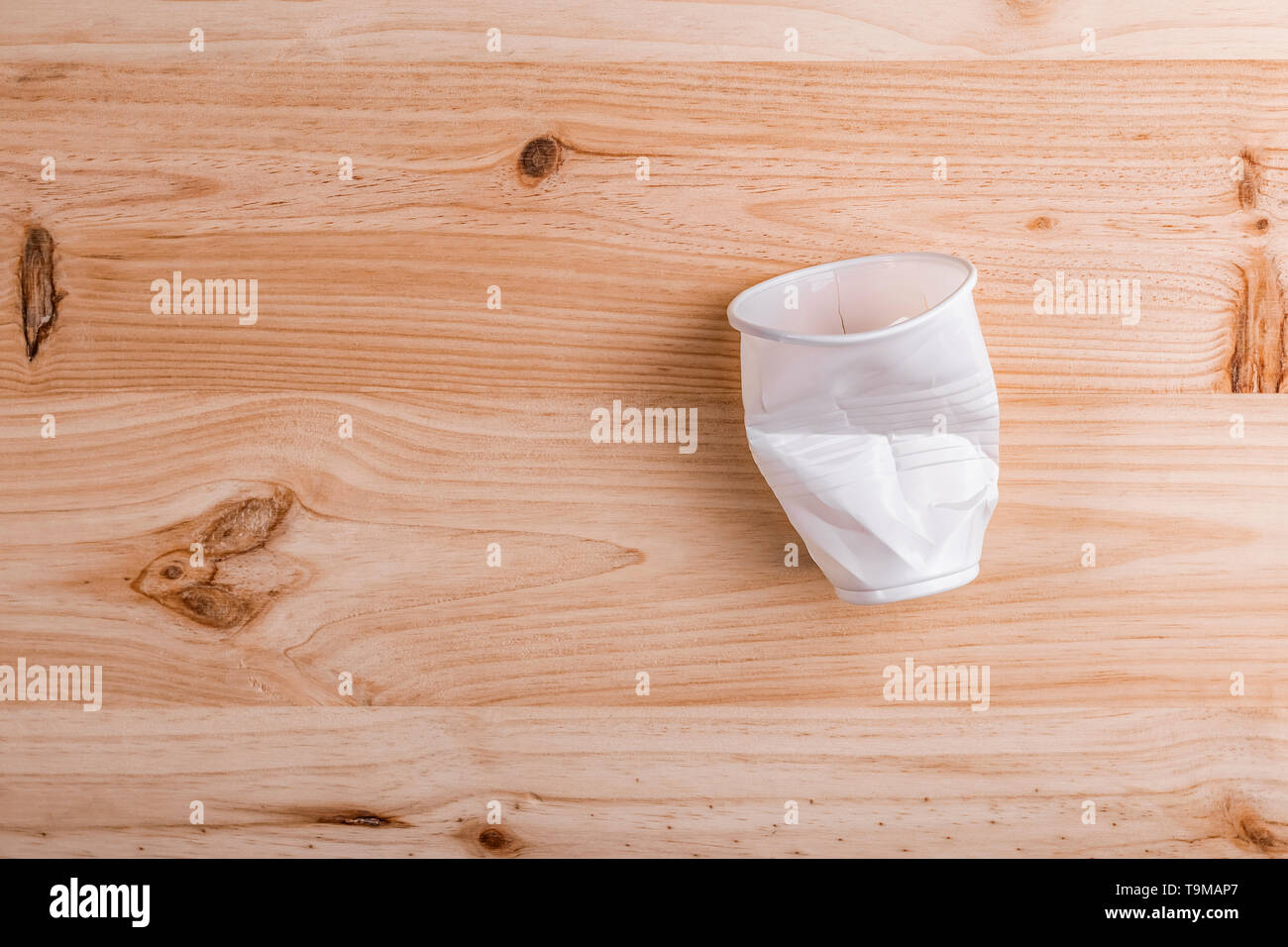 Broken crumpled white plastic Cup lies on a wooden table of natural ...