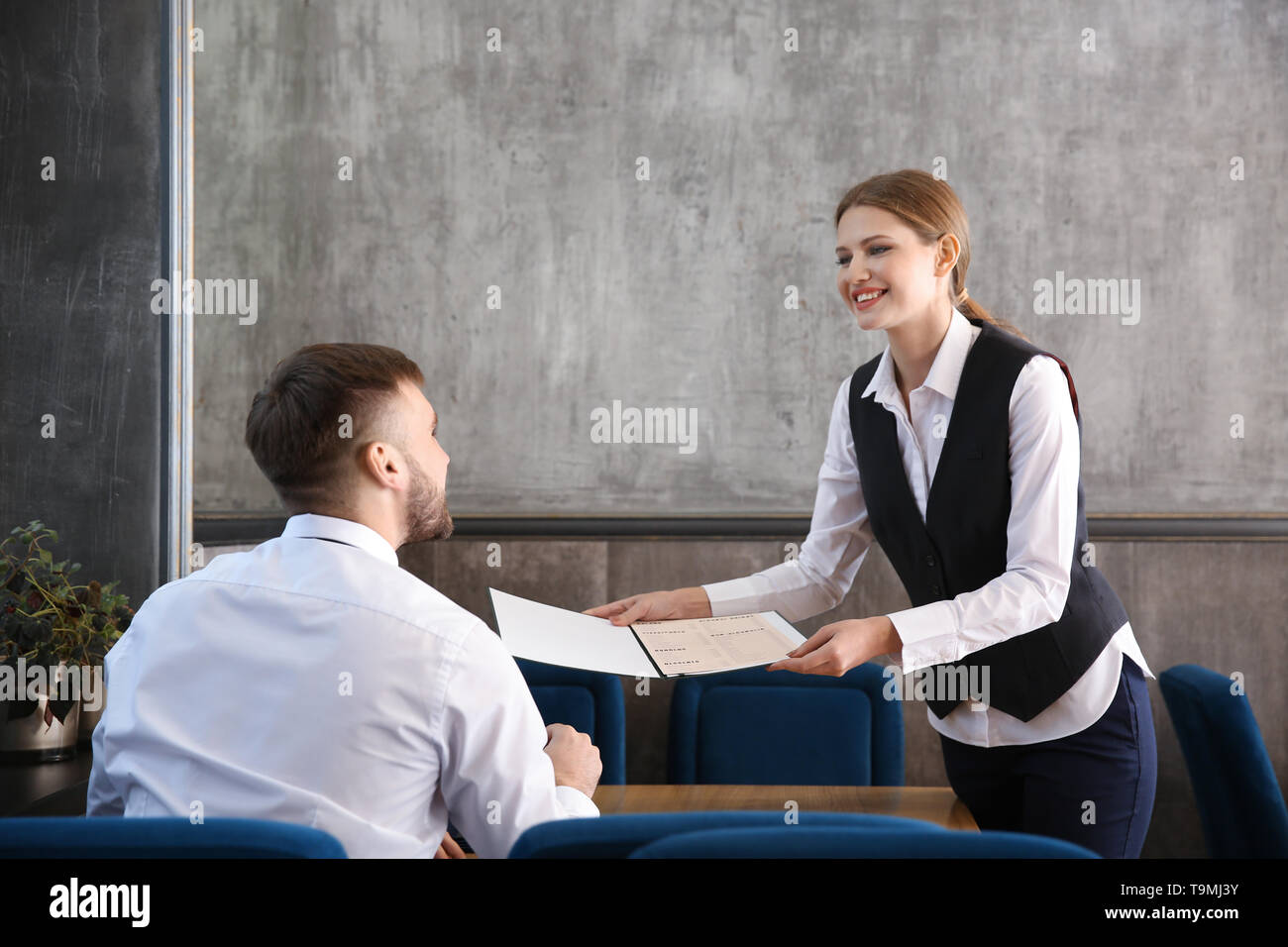 Young waitress showing man a menu in restaurant Stock Photo - Alamy