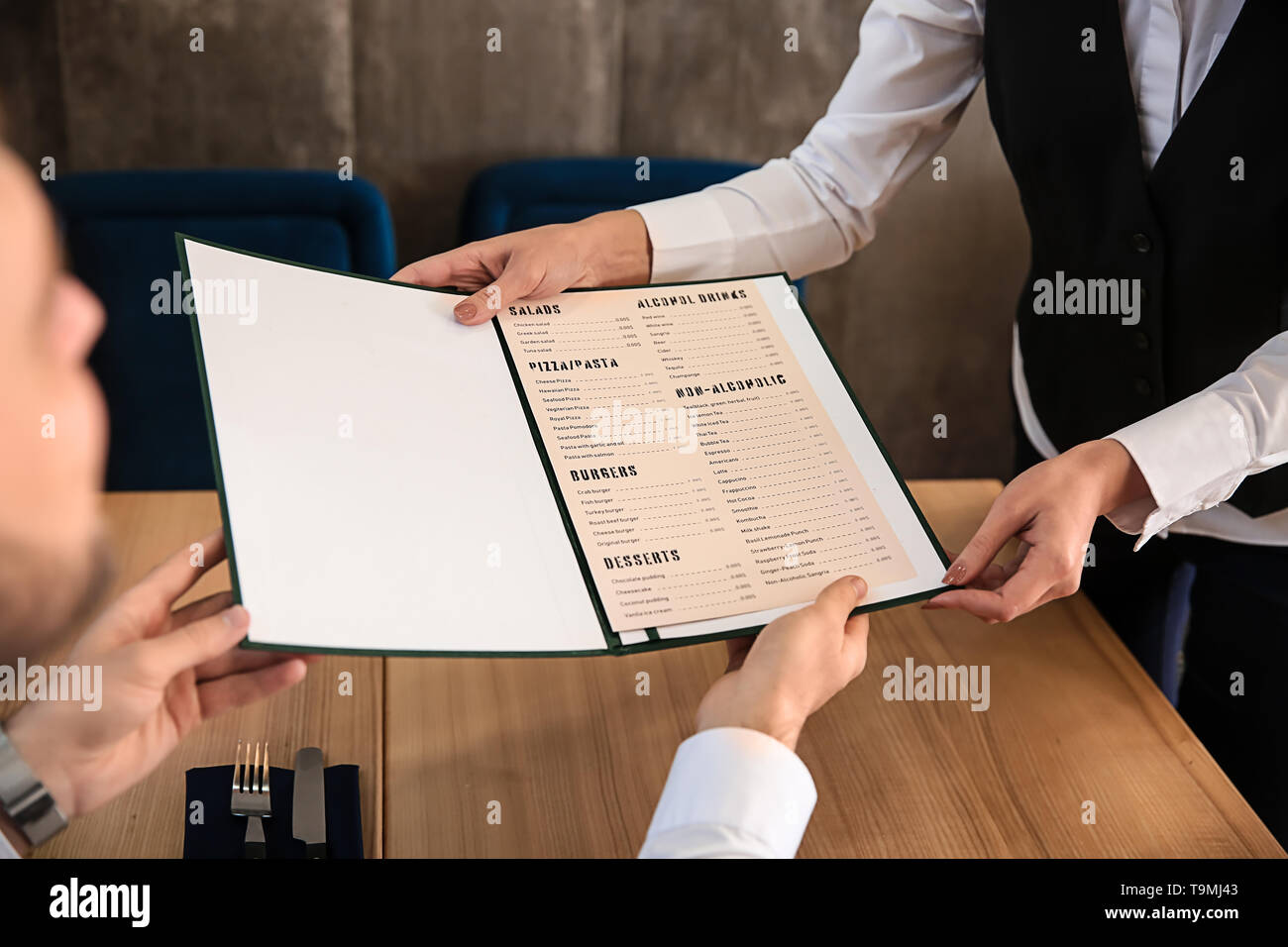 Young waitress showing man a menu in restaurant Stock Photo - Alamy