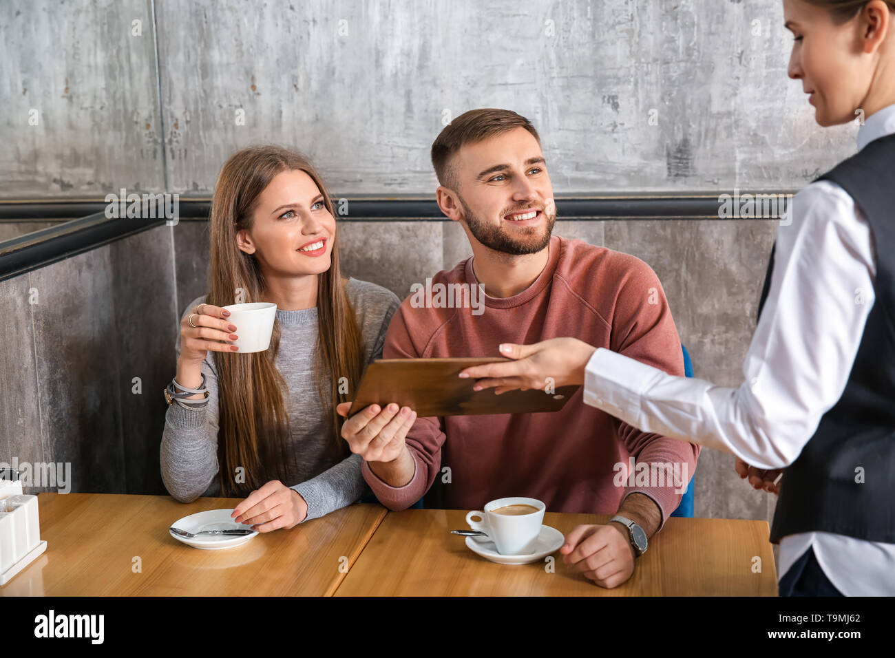 Waitress showing young couple a menu in restaurant Stock Photo - Alamy
