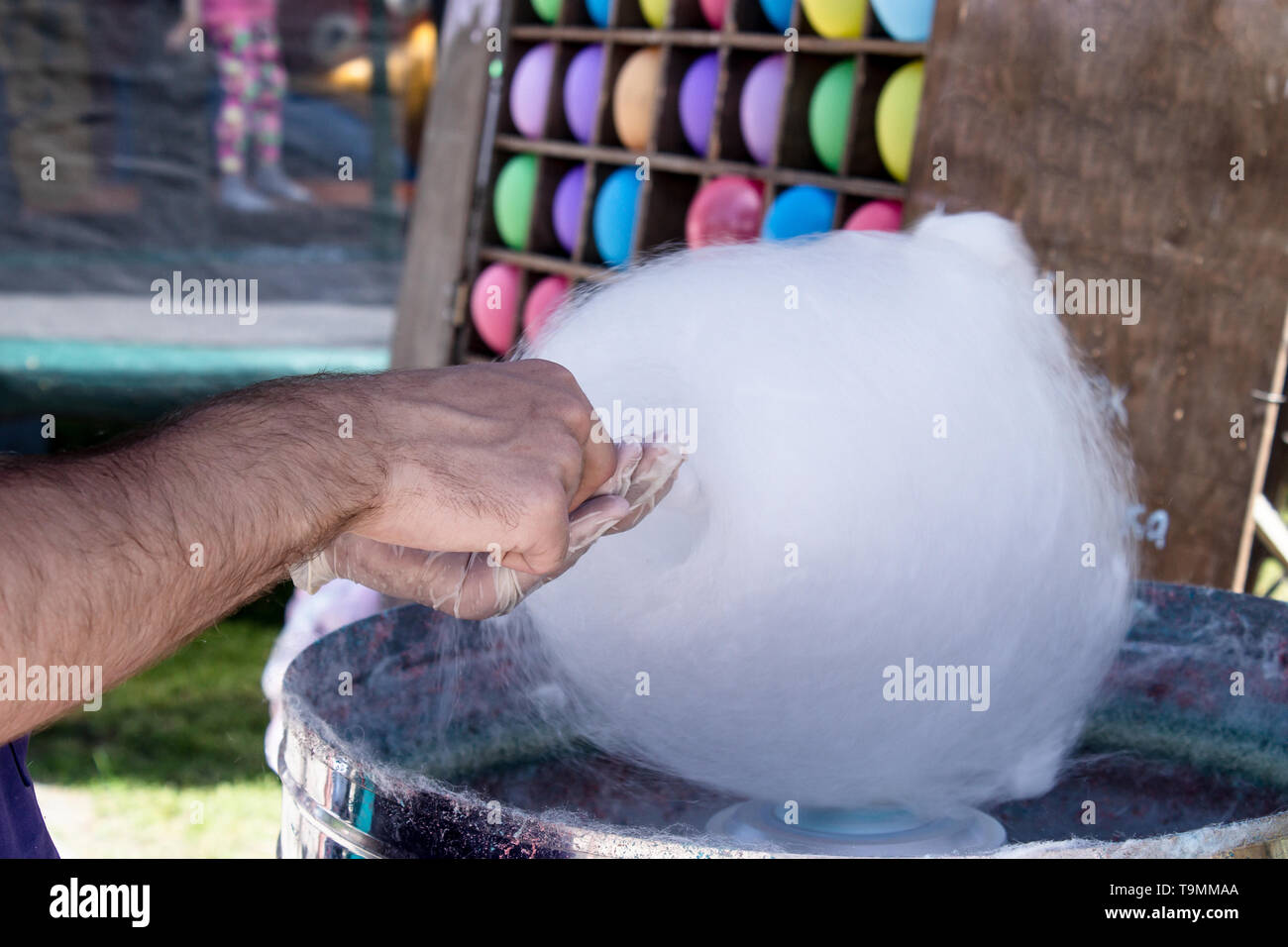 A hand wrap a cotton candy on a stick in a cotton candy machine. Making ...