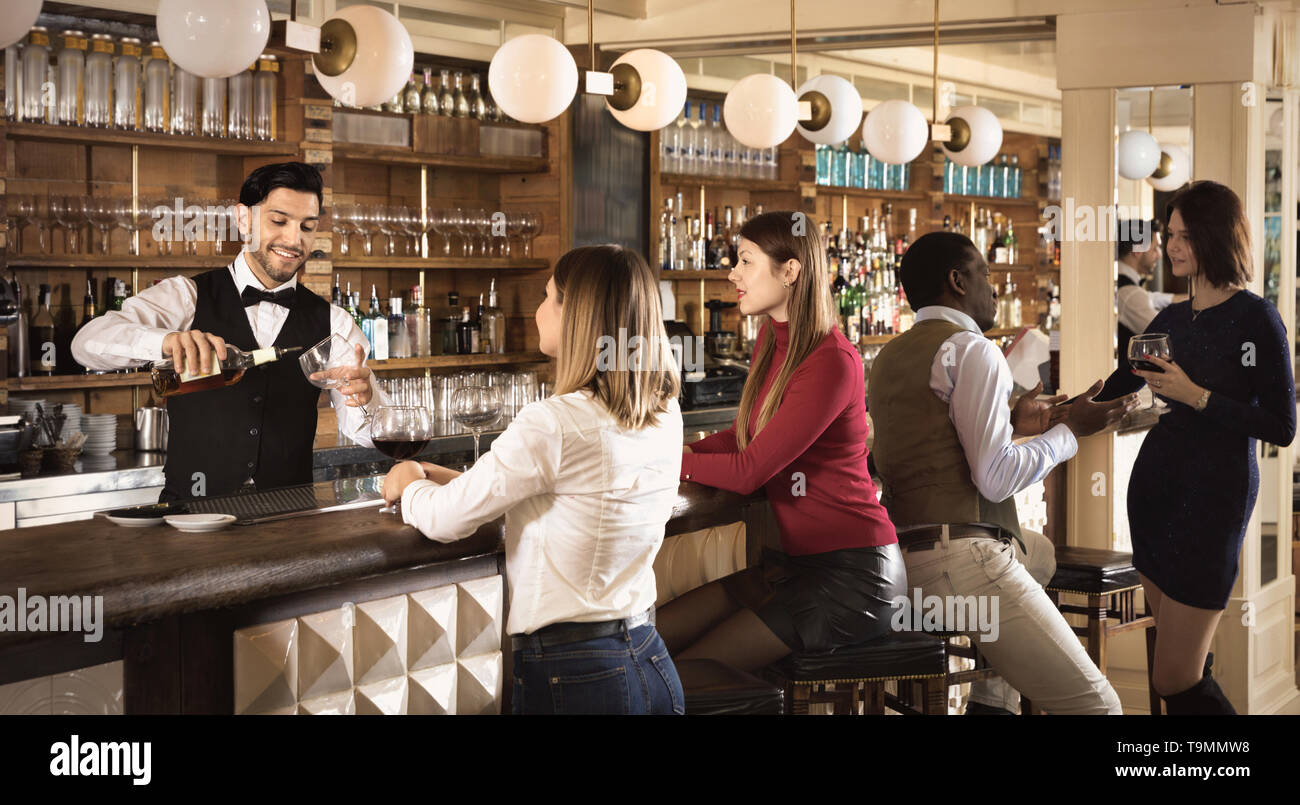 Happy cheerful positive barman is servicing young people who are ...