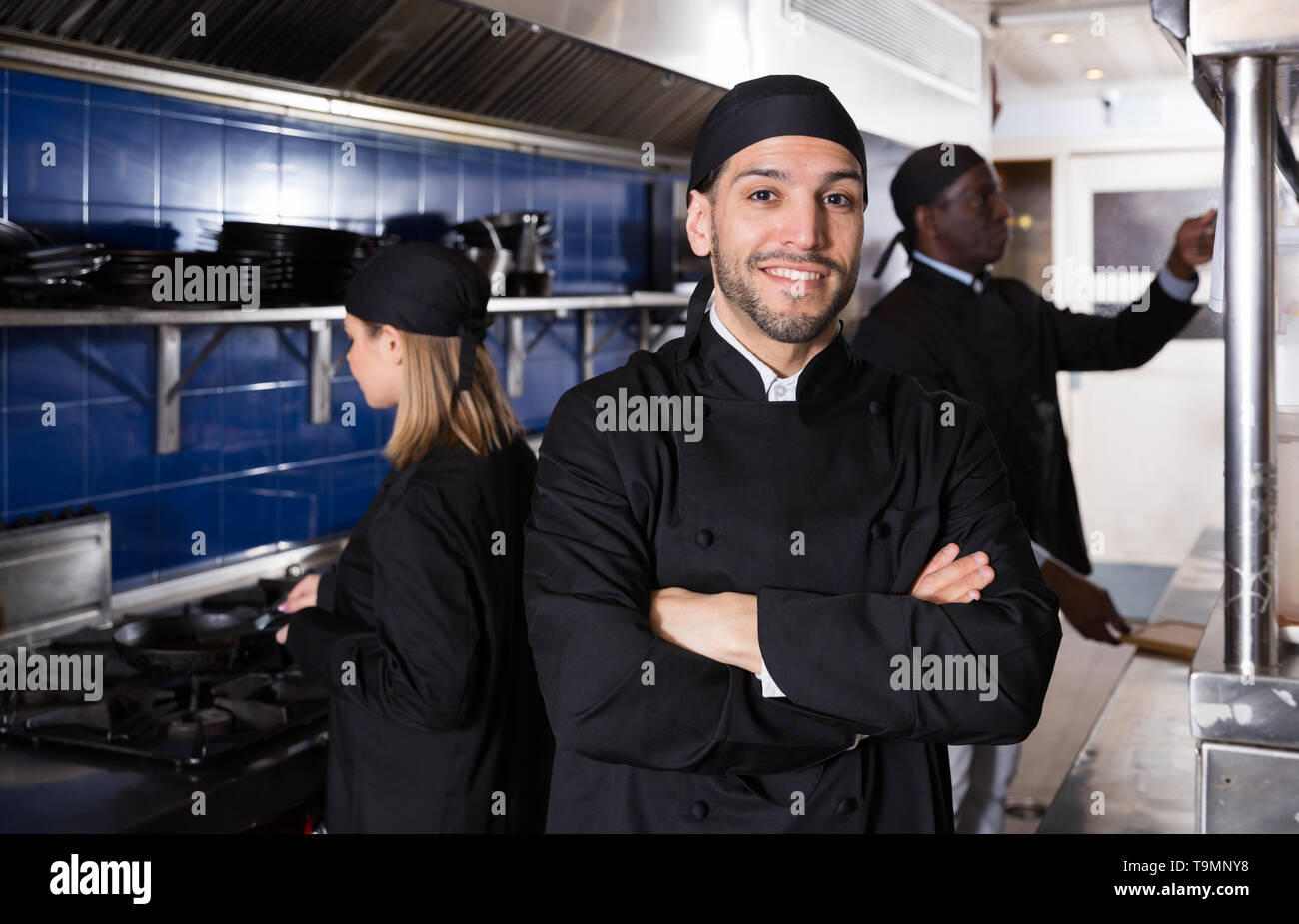 Confident chef of restaurant posing with arms crossed in kitchen on ...