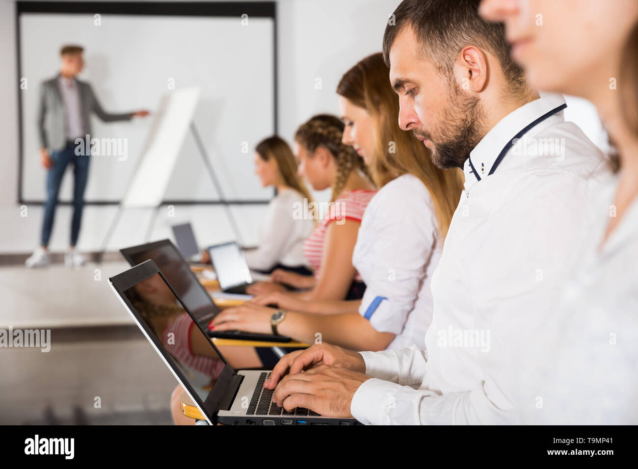 Side view of row of people sitting with laptops, listening lecturer at ...