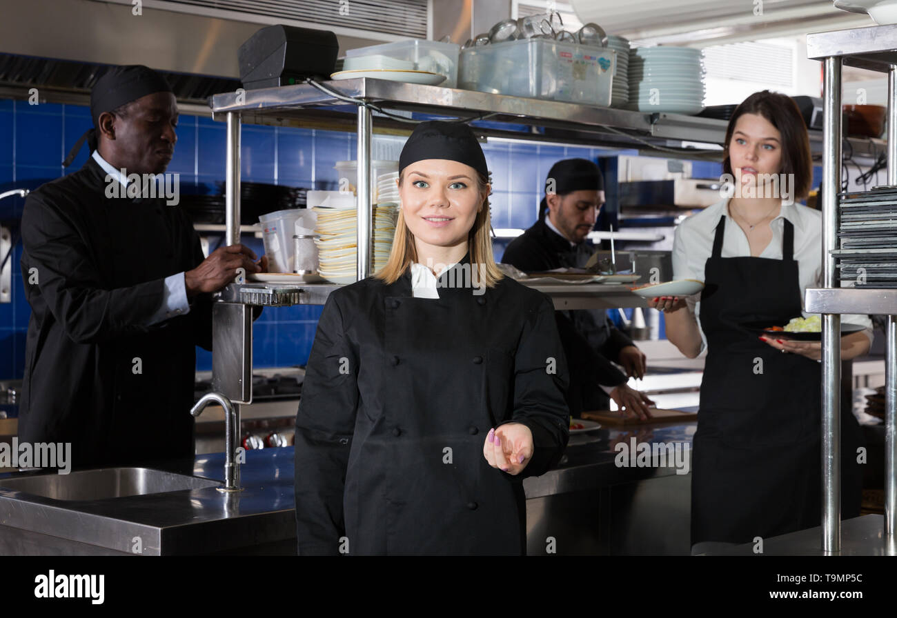 Attractive female chef of restaurant standing in professional kitchen ...