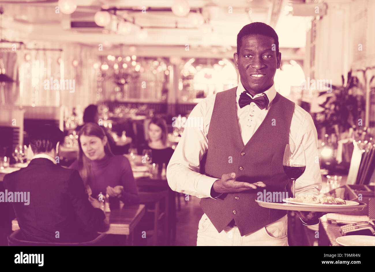 Smiling positive man waiter is holding tray with order in hall of ...