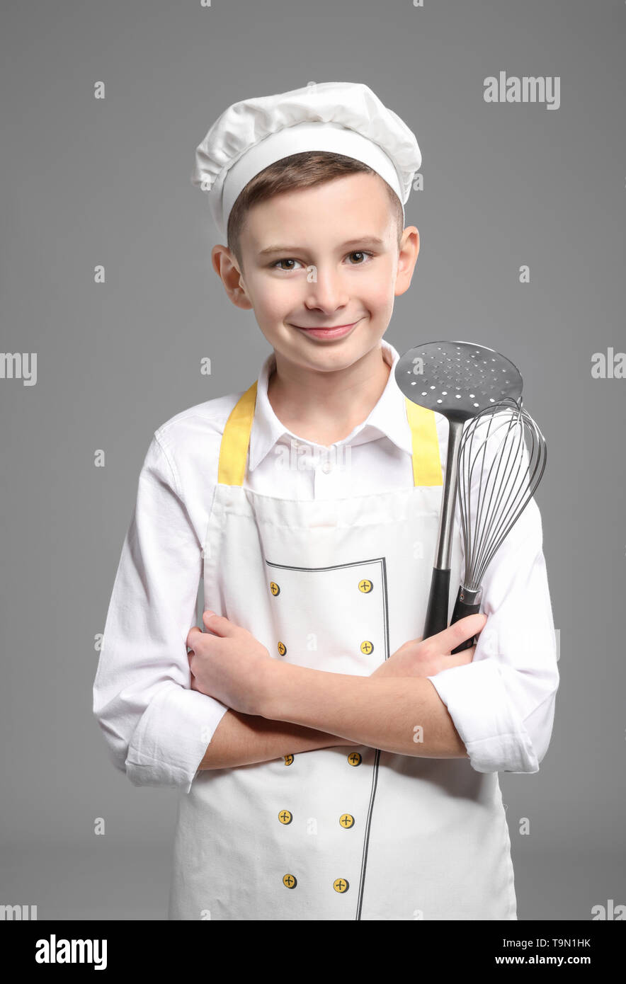 Cute little chef with kitchen utensils on grey background Stock Photo ...