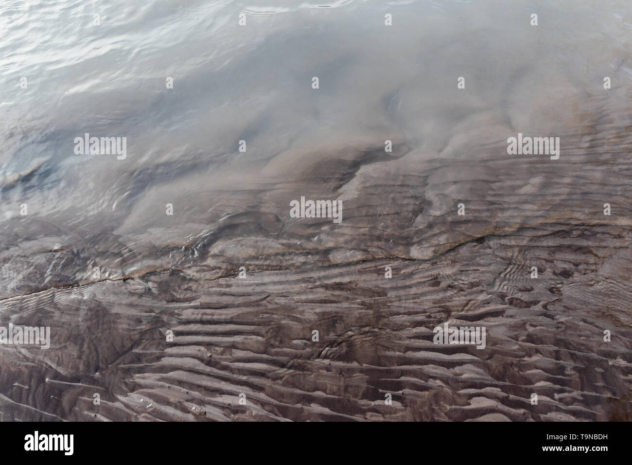 Glacial riverbank shore with wet black silt sand mud water channels ...