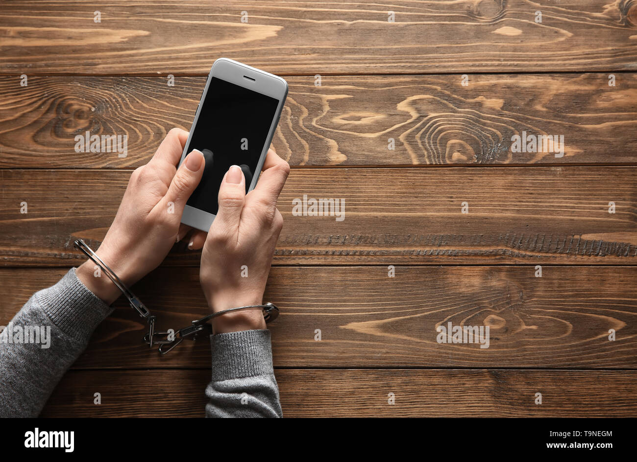 Female hands in handcuffs with mobile phone on wooden background ...