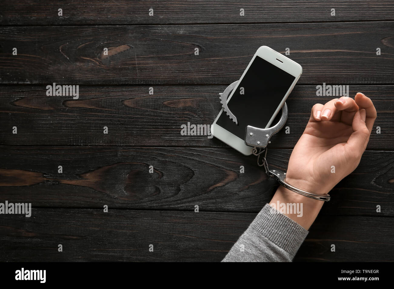 Female hand in handcuffs with mobile phone on wooden background ...