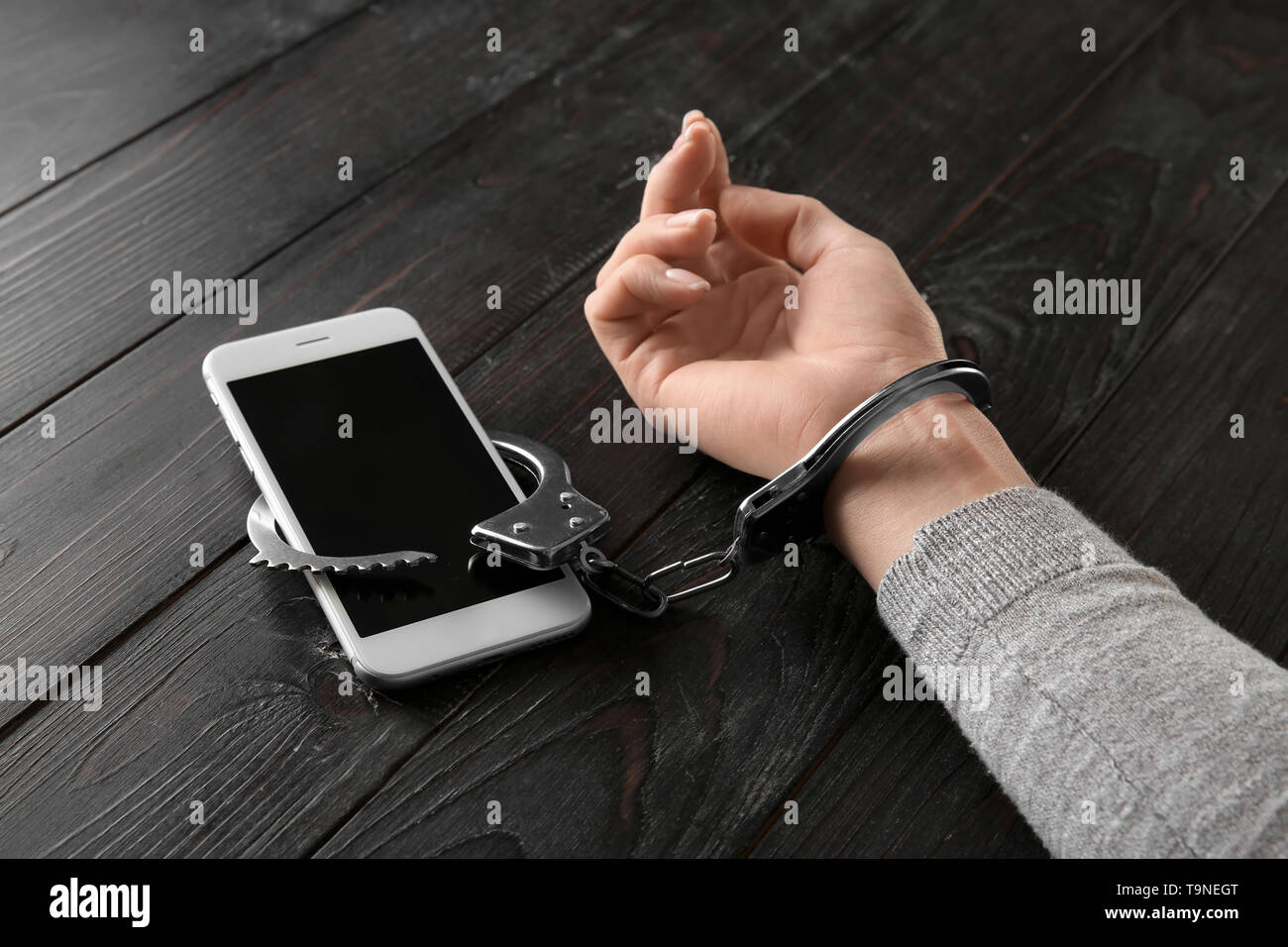 Female hand in handcuffs with mobile phone on wooden background ...