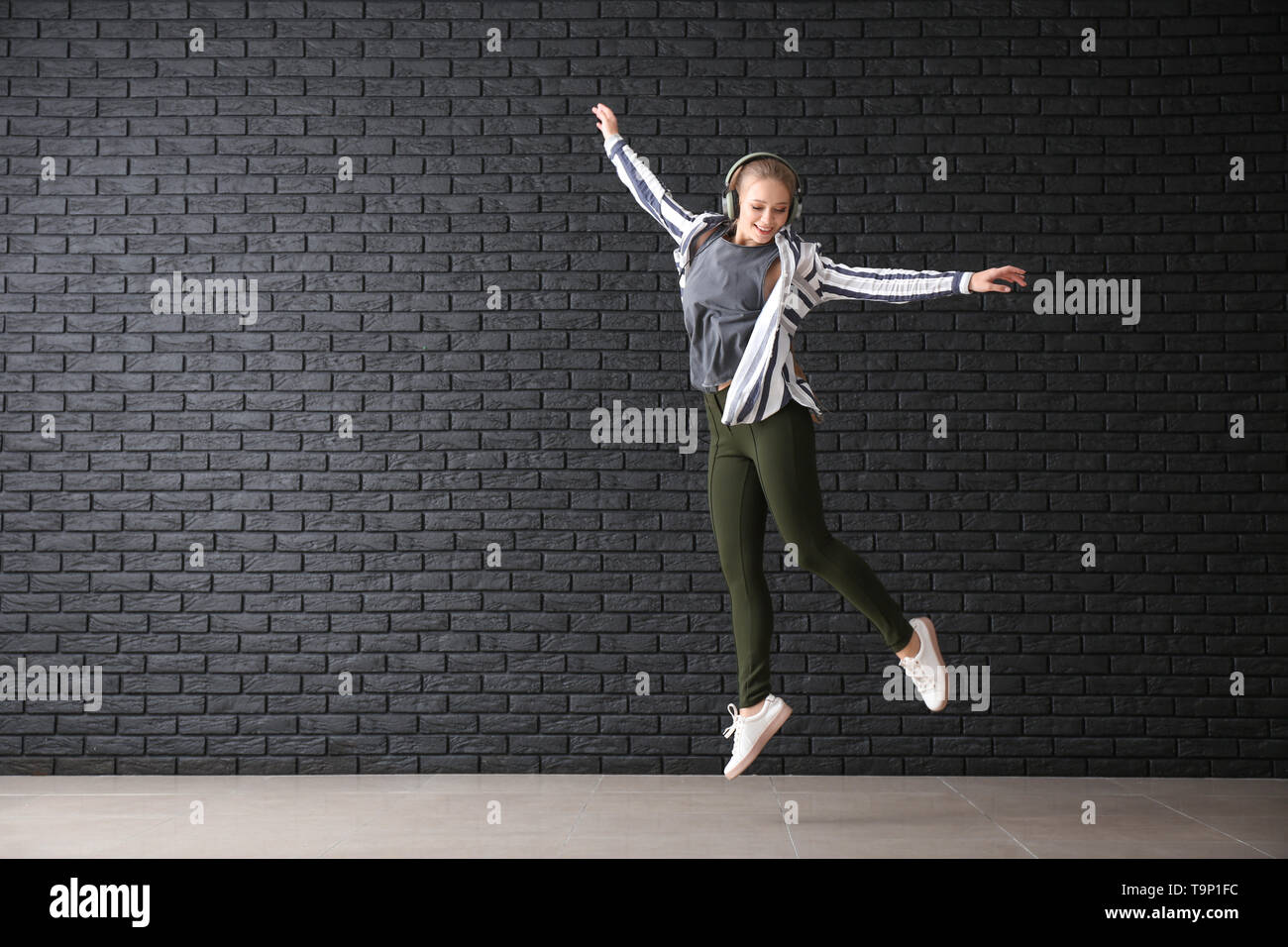 Beautiful young woman dancing against dark brick wall Stock Photo - Alamy