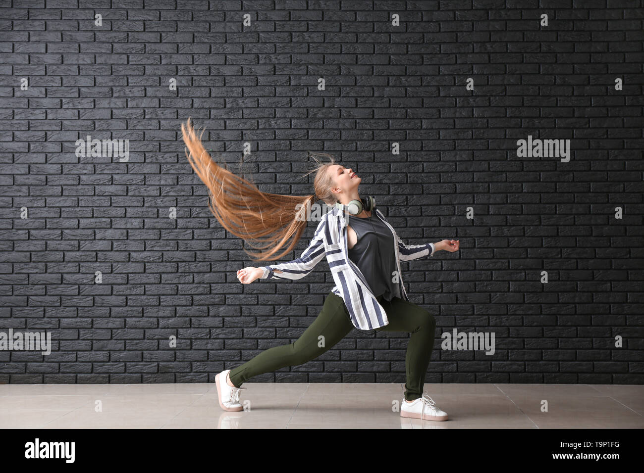 Beautiful young woman dancing against dark brick wall Stock Photo - Alamy