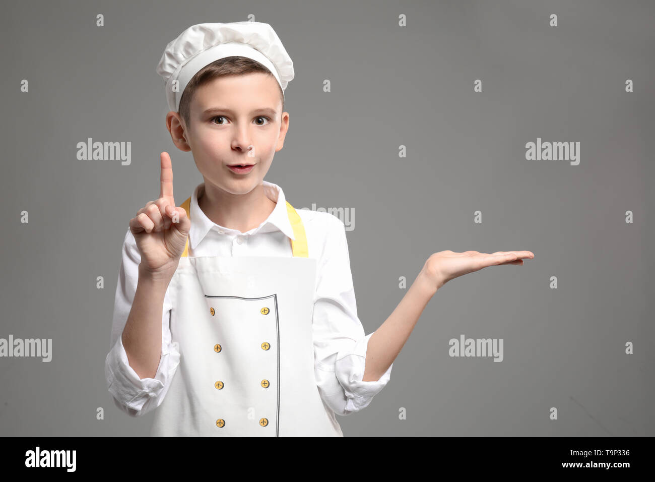 Cute little chef with raised index finger holding something on grey ...