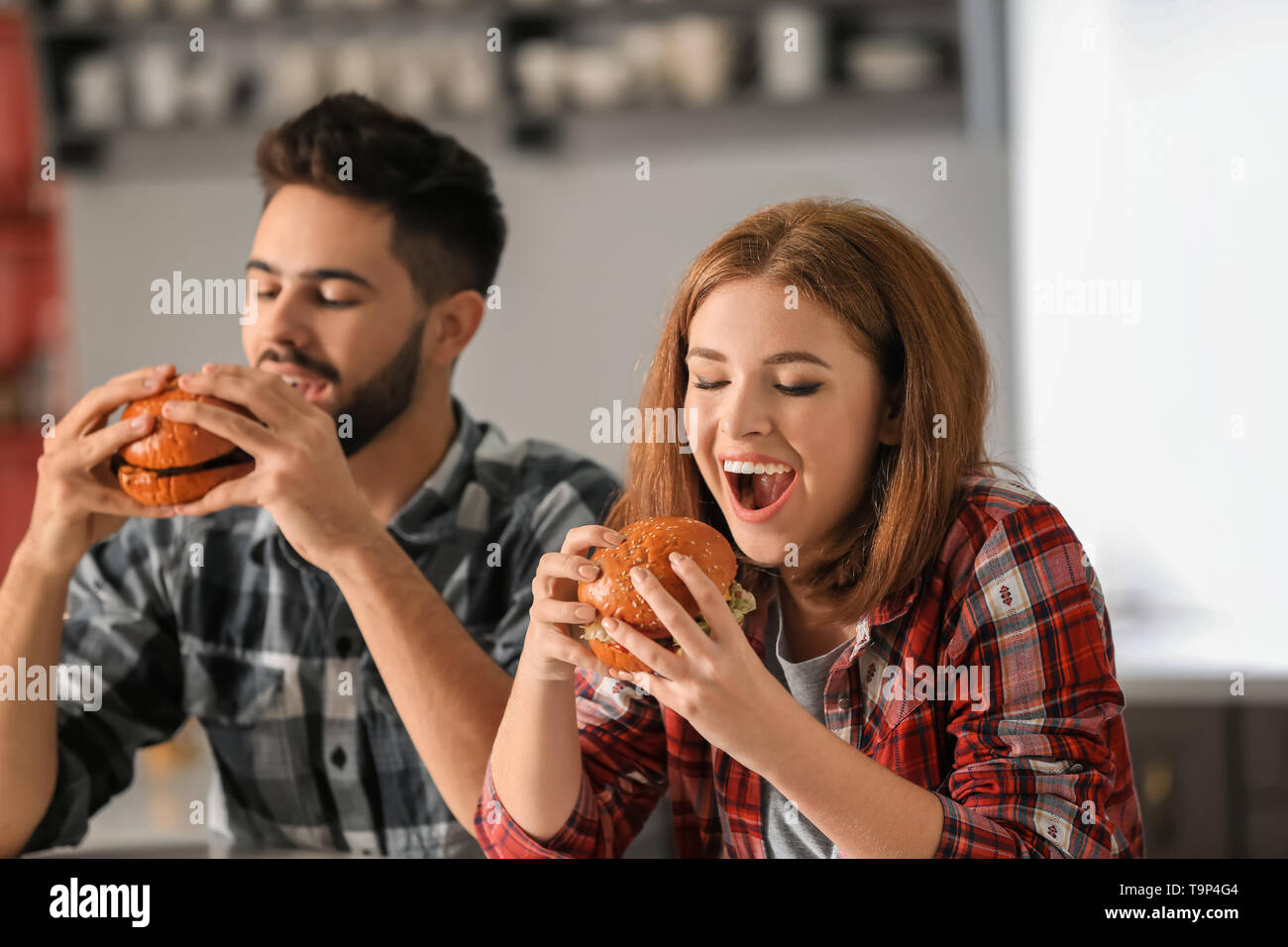 Young couple eating tasty burgers at home Stock Photo - Alamy