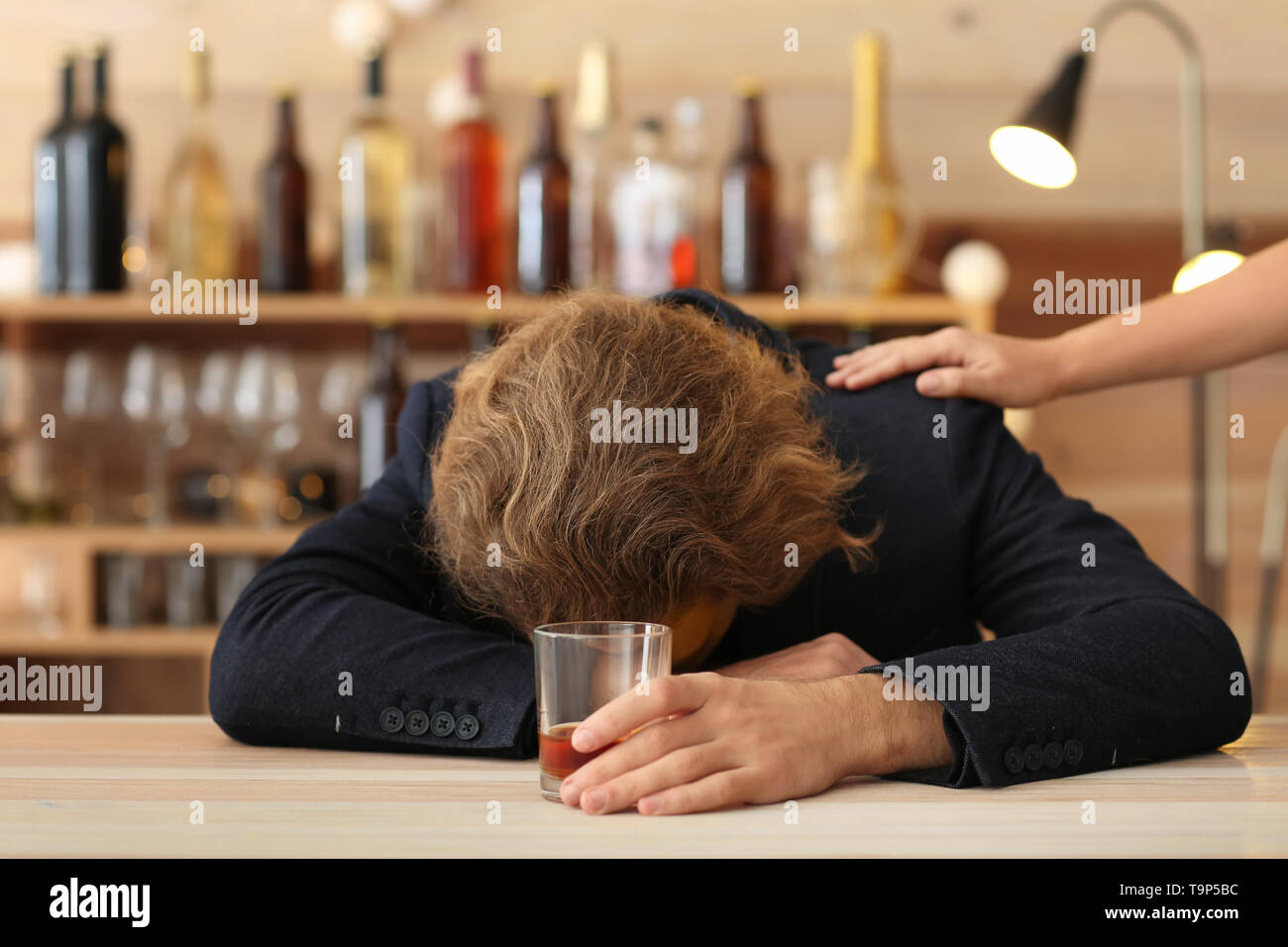 Woman trying to wake up drunk man with glass of whiskey in bar ...