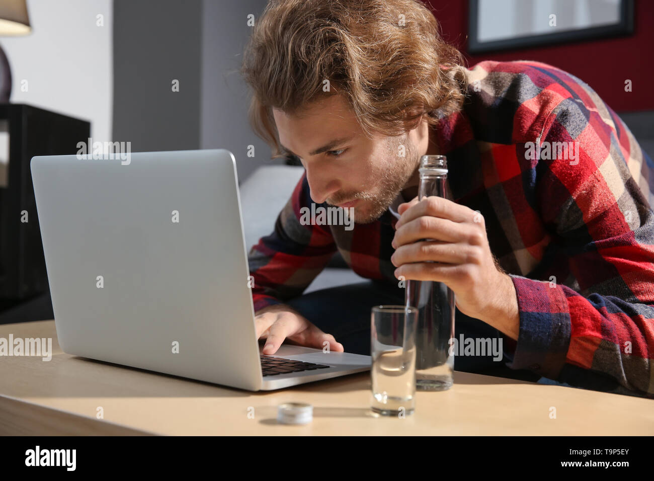 Young man using laptop and drinking vodka at home. Alcoholism concept ...