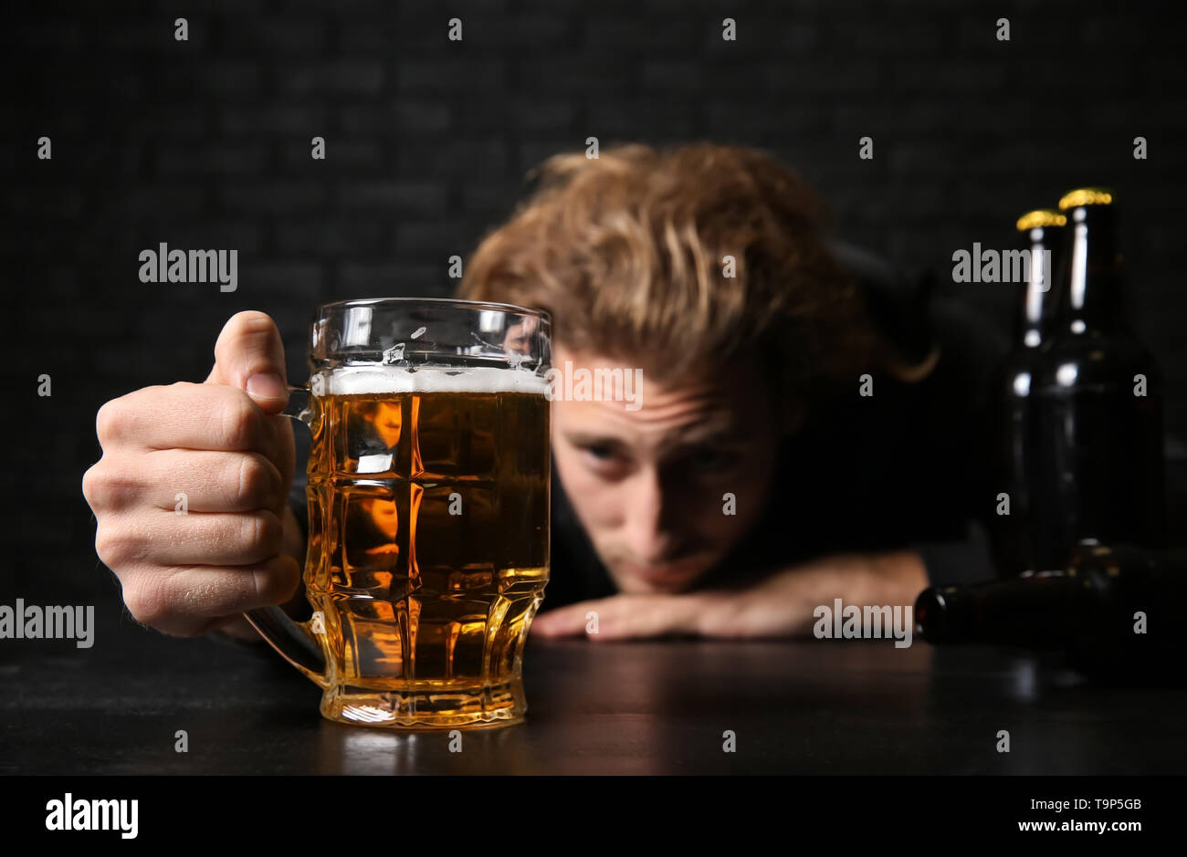Drunk young man with beer at table near black brick wall. Alcoholism ...