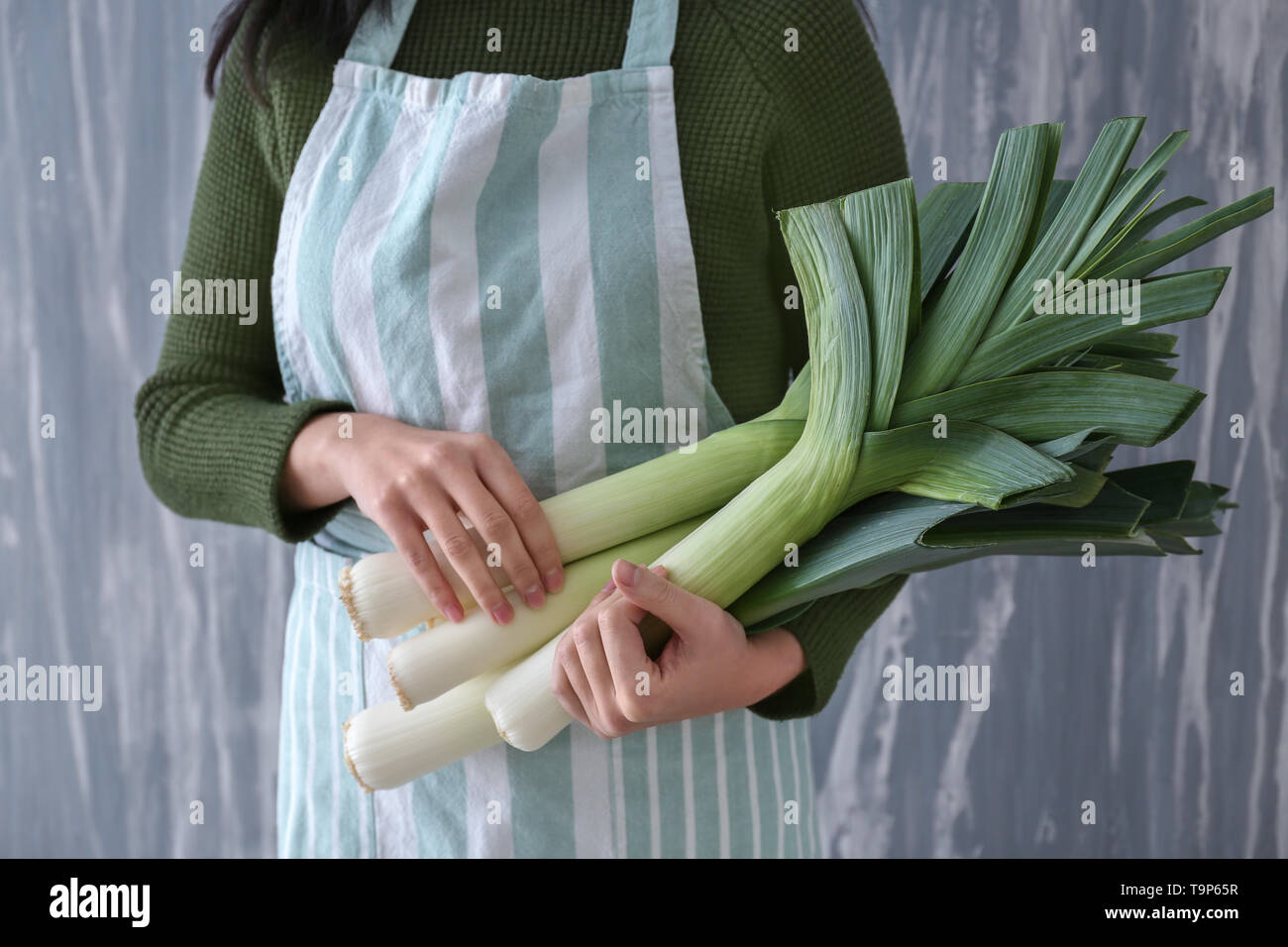 Woman holding raw leeks against grey background Stock Photo - Alamy