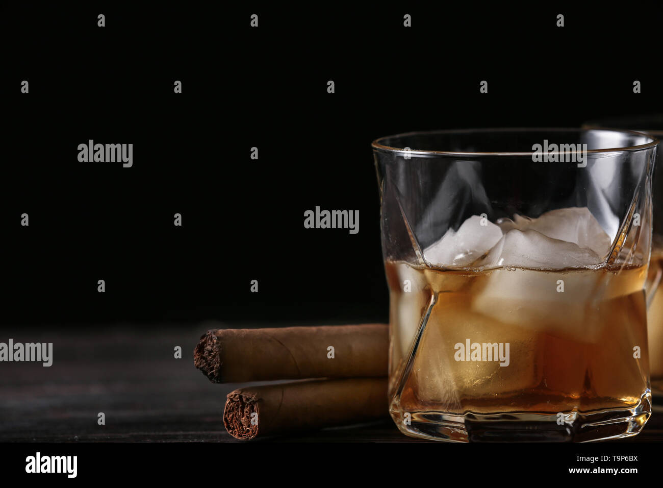 Glass of cold whiskey with cigars on wooden table against dark ...