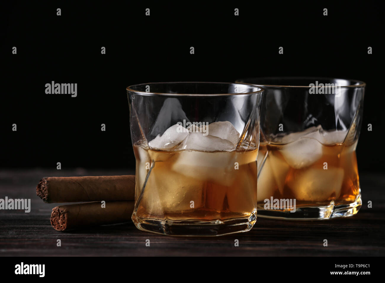 Glasses of cold whiskey with cigars on wooden table against dark ...