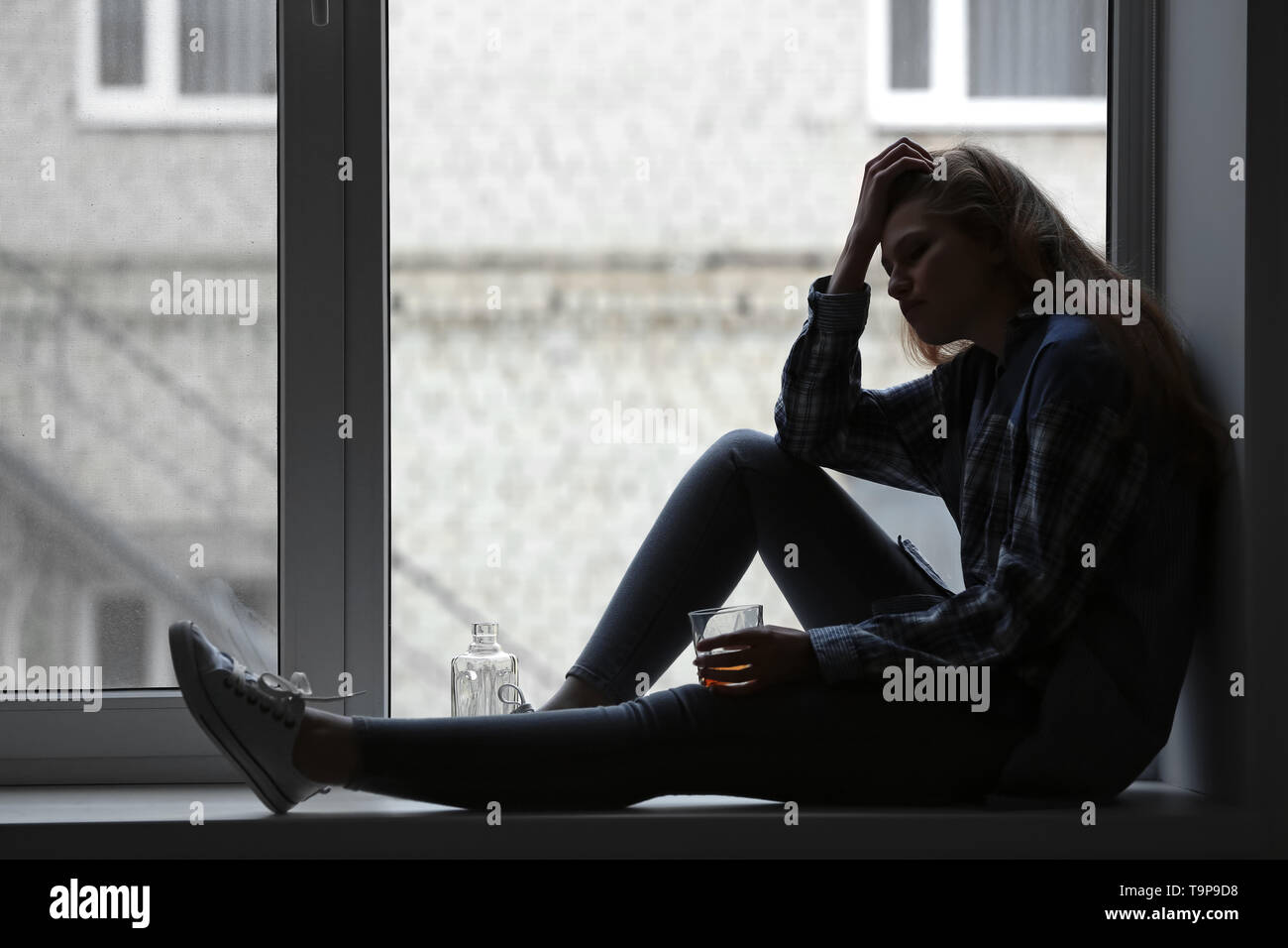 Depressed woman drinking alcohol near window Stock Photo - Alamy
