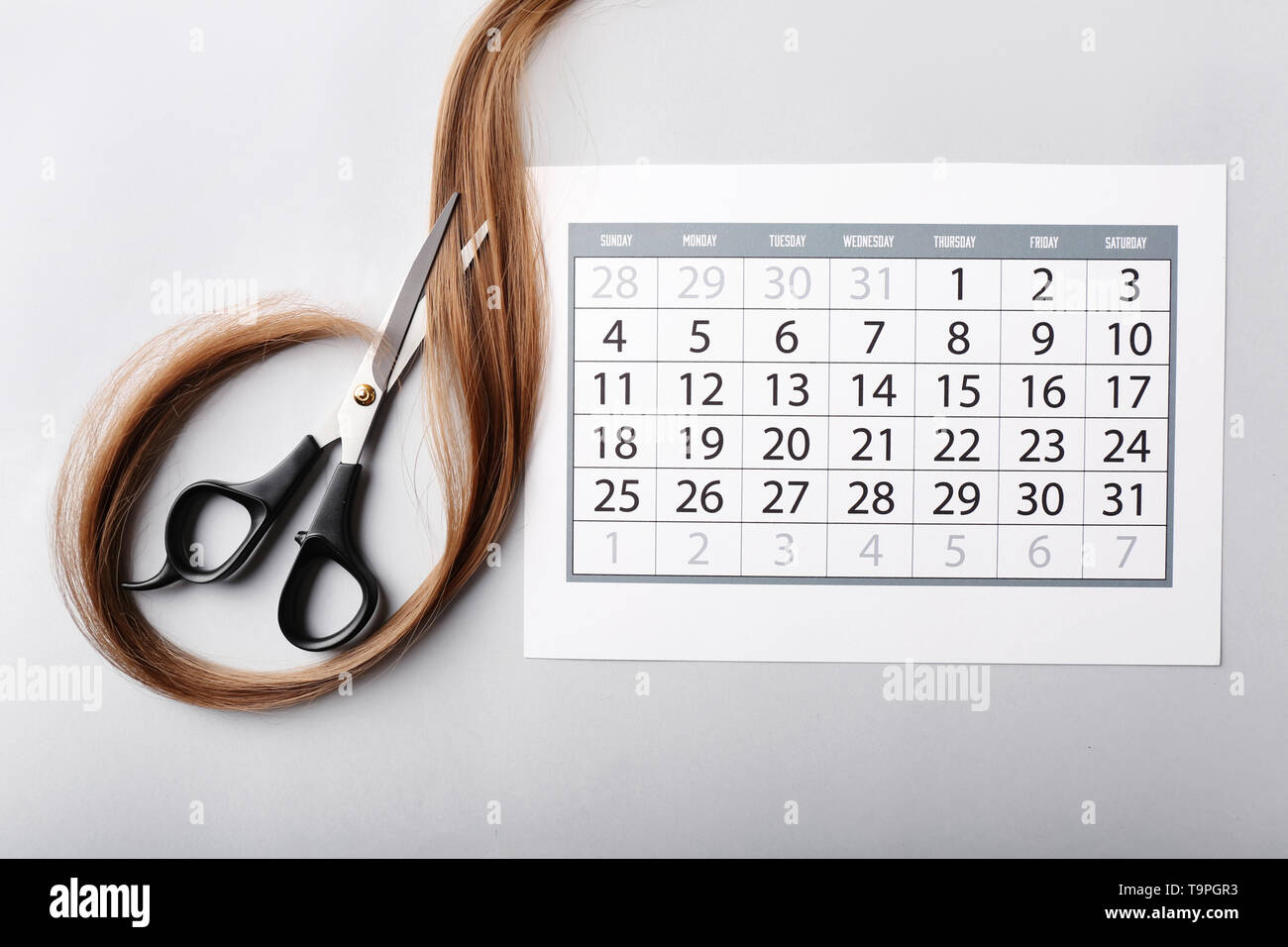Calendar with hairdresser's scissors and strand on light background ...