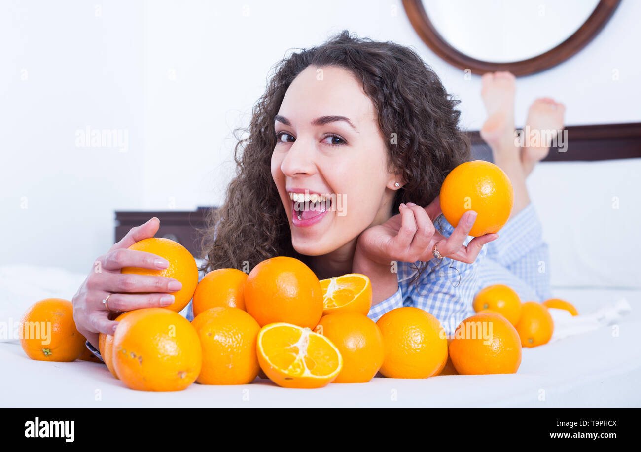 Cheerful female brunette eating oranges in bedroom interior Stock Photo ...