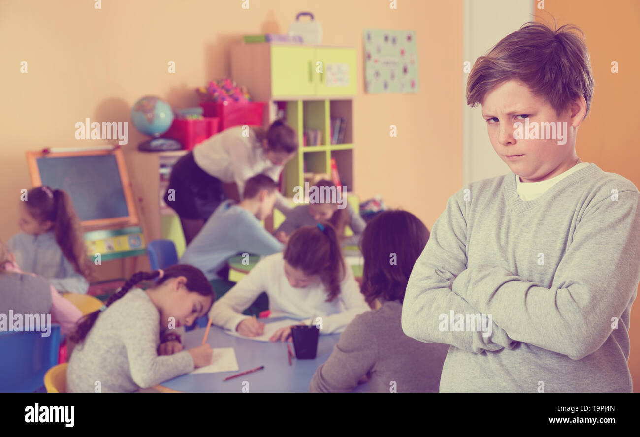 Portrait of upset angry boy in schoolroom on background with pupils ...