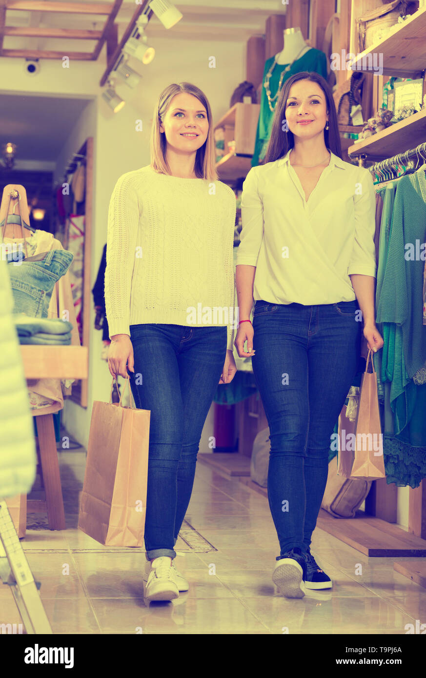 Smiling young women carrying paper bags with purchases in fashion store ...