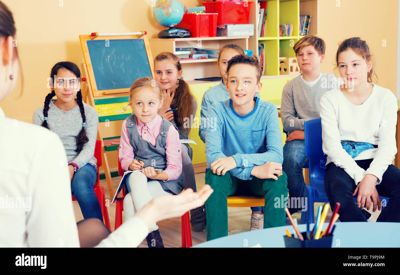 Happy boys and girls listening teacher, sitting at lesson in classroom ...