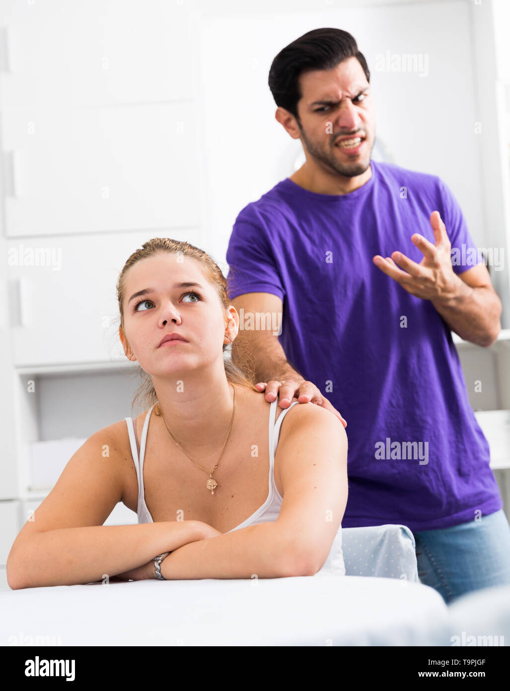 Upset young woman sitting at home table with disgruntled man behind ...