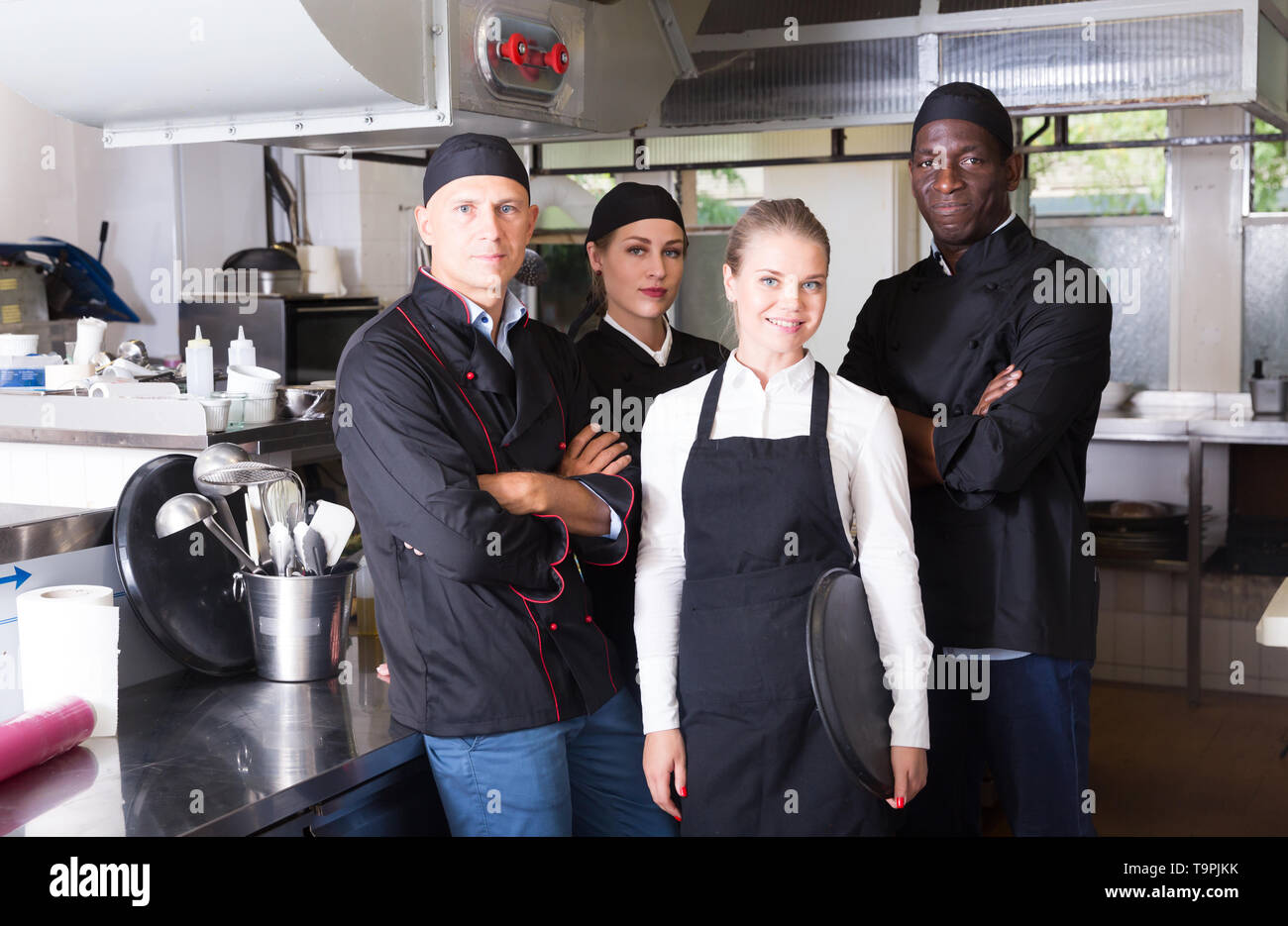Portrait of confident smiling team of chefs in interior of restaurant ...