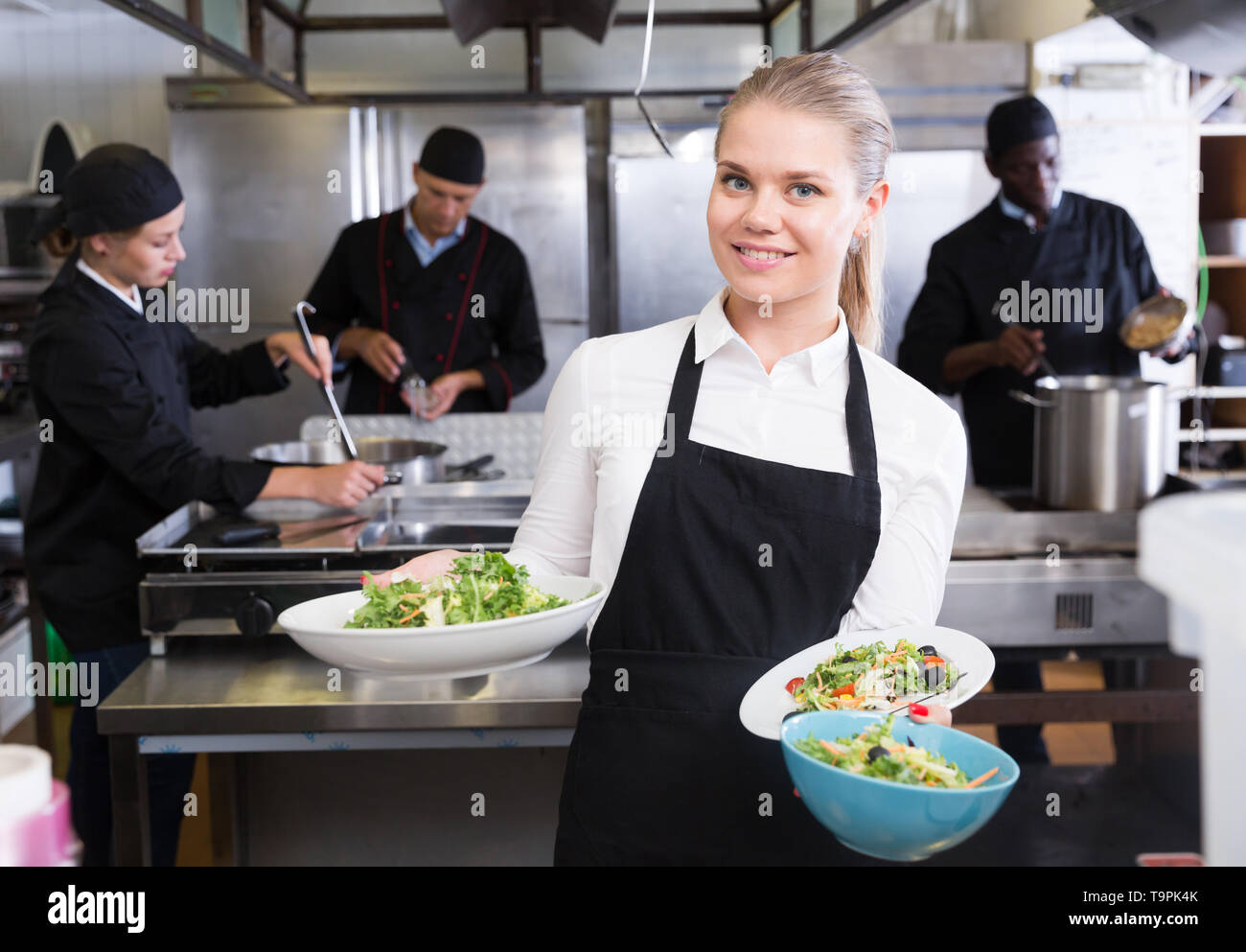 Successful young waitress standing in restaurant kitchen with ordered ...